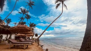 Uma praia com palmeiras, cabanas de teto de palha e cadeiras de descanso.