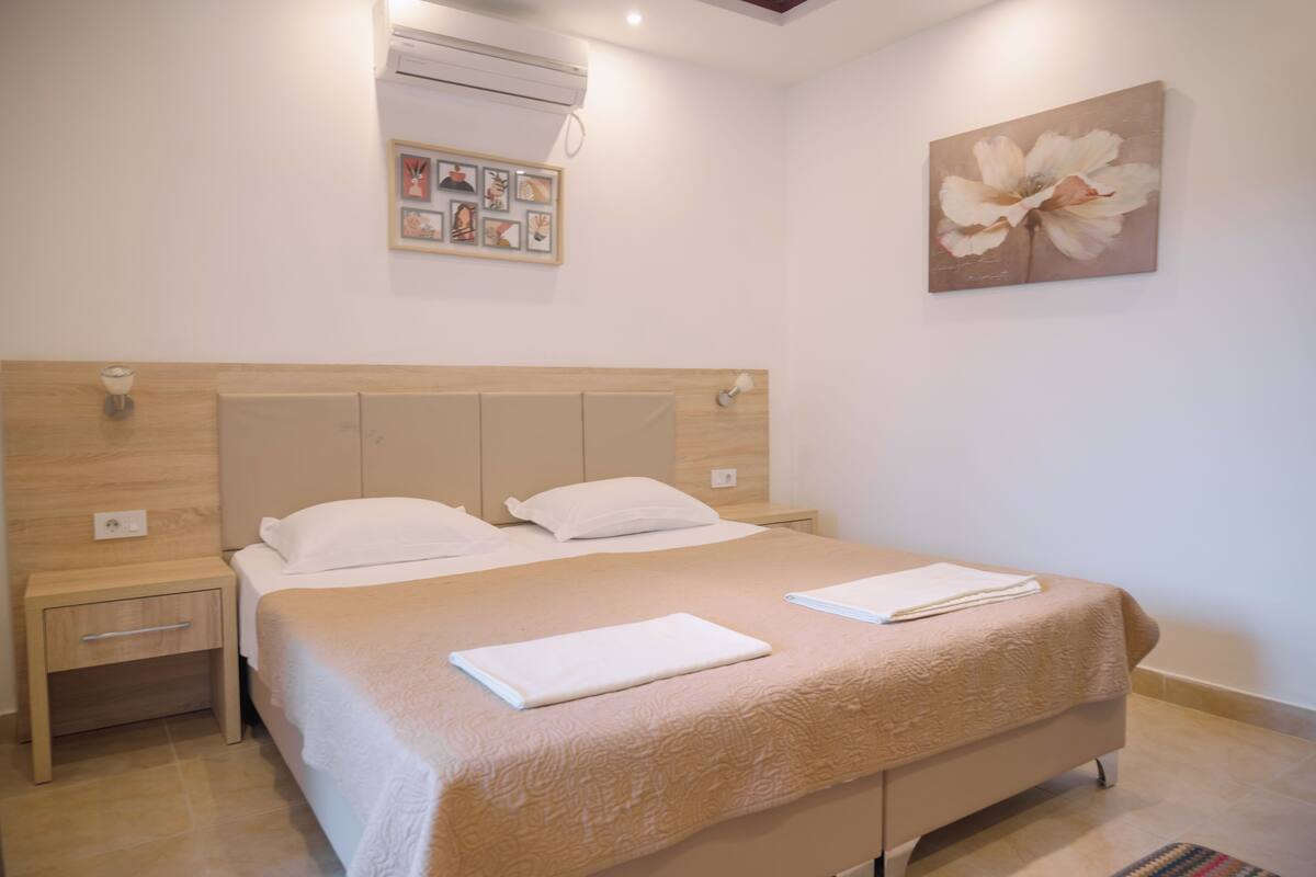 Quarto com cama, mesas de cabeceira, ar-condicionado fixado na parede e um quadro emoldurado.
