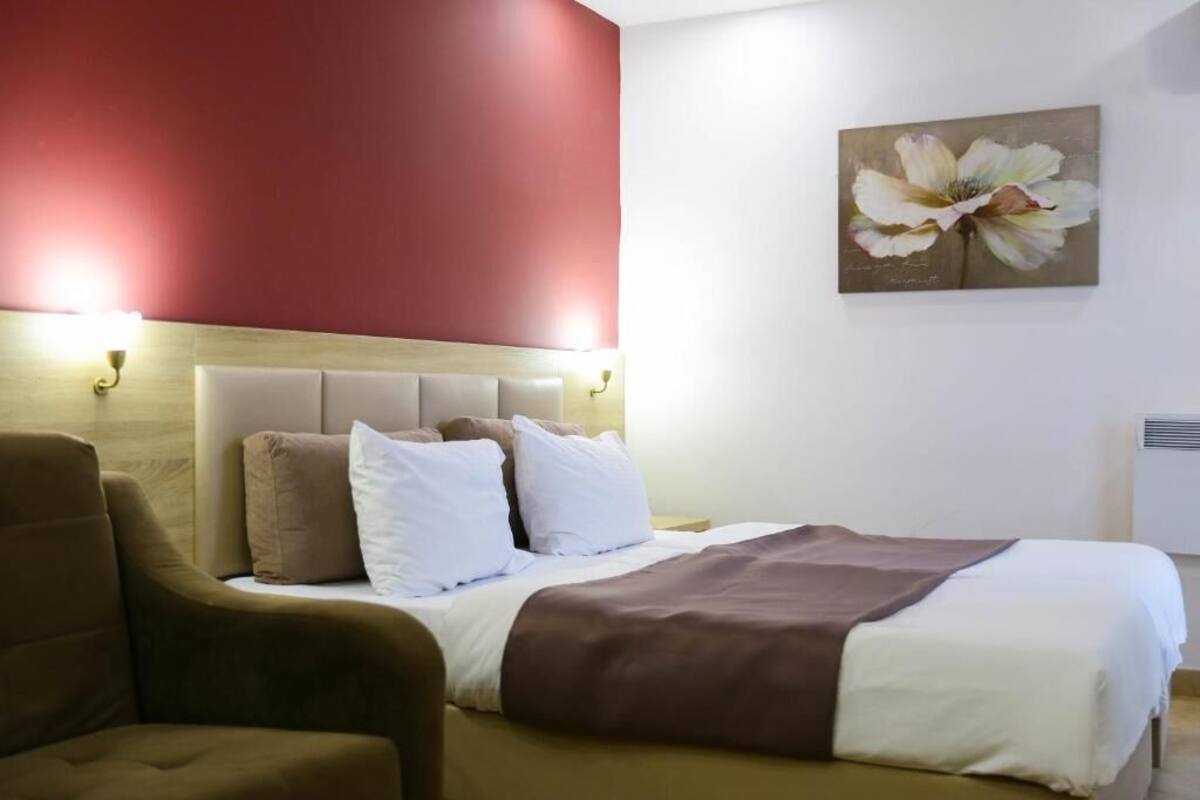 Quarto de hotel com uma cama, uma poltrona marrom e um quadro de uma flor na parede.