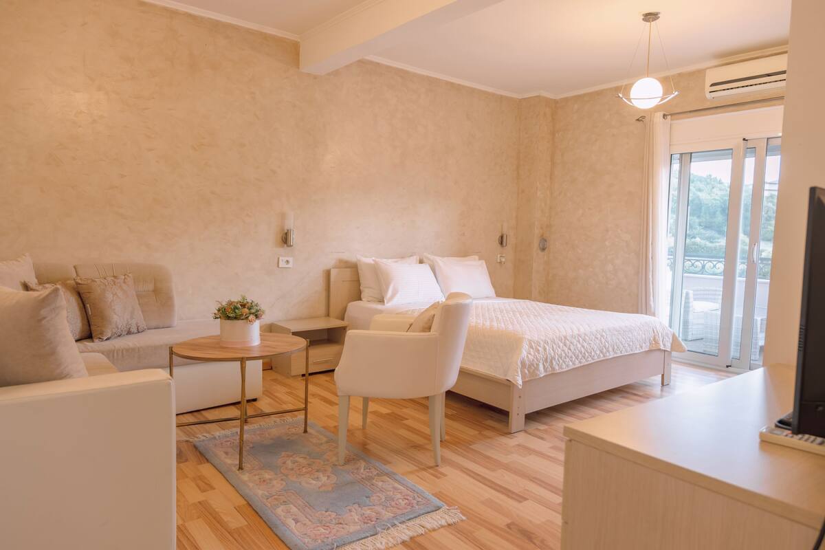 Quarto com cama, sofá, poltrona, mesinha com planta e televisão.