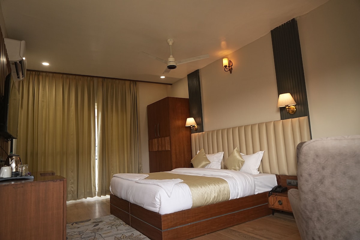 Quarto de hotel com uma cama grande, uma escrivaninha, uma cadeira, um ventilador de teto e um abajur fixado na parede.