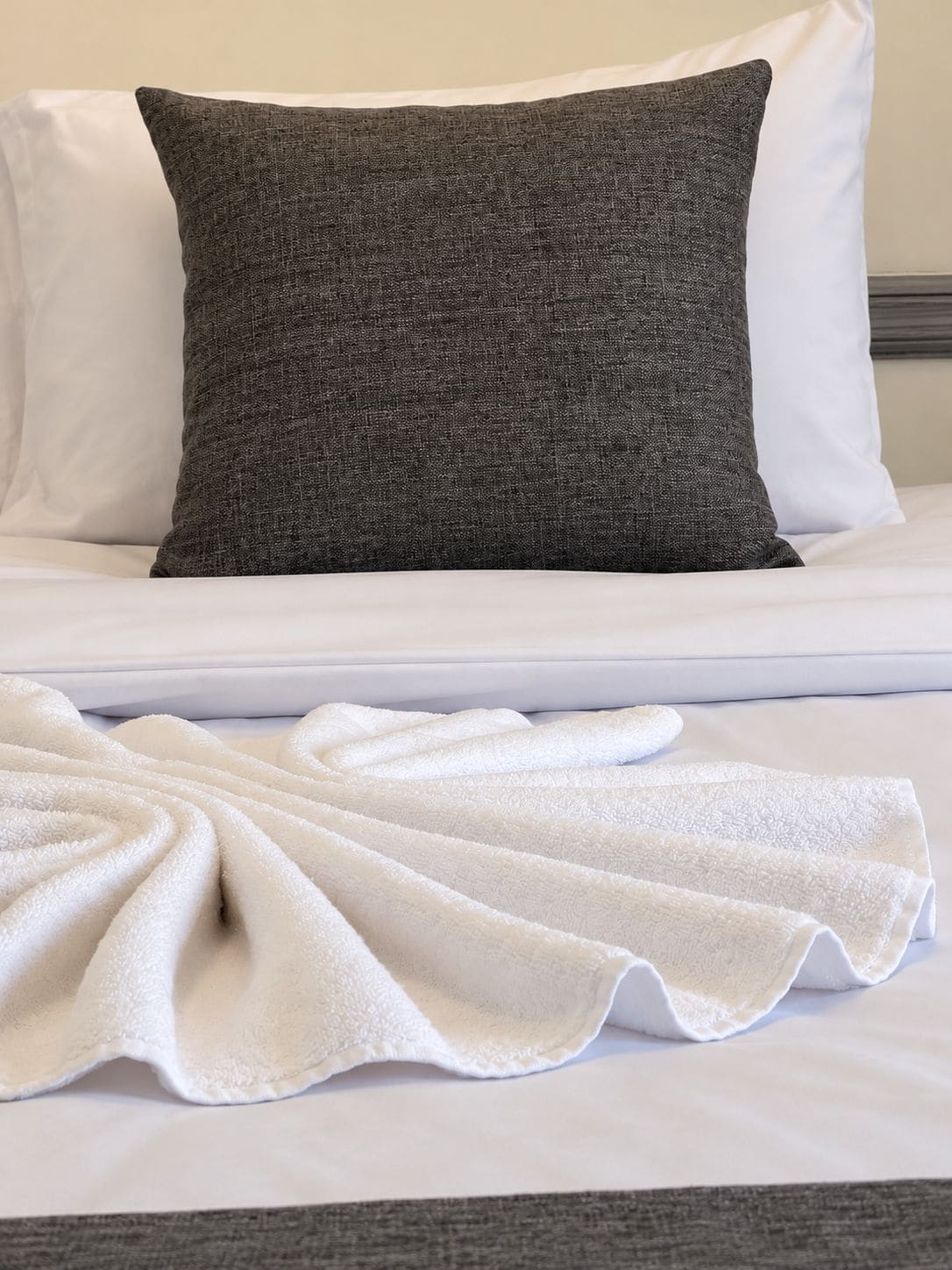 Cama bem arrumada com travesseiro cinza e toalha branca.