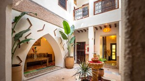 Um pátio interno com piso de azulejos, plantas em vasos, um banco e uma escadaria para um andar superior.