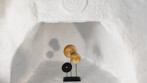 Paredes brancas texturizadas com um nicho que contém um pequeno suporte preto e dois objetos decorativos dourados.