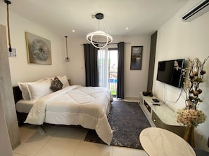 Quarto moderno com cama, televisão, escrivaninha e uma janela grande.