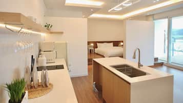 Quarto de hotel moderno com cozinha compacta, cama com encosto e vista através de uma porta de vidro.