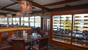 Restaurante com uma grande mesa de jantar, cadeiras e uma estante de vinhos visíveis através de um muro de vidro.