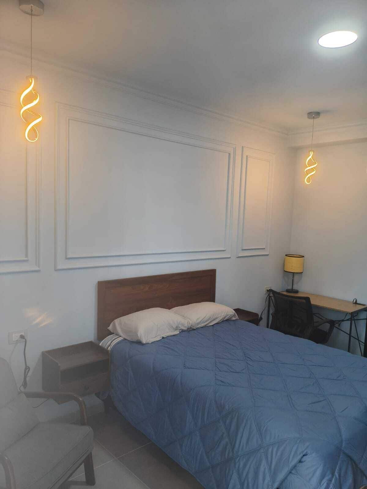 Quarto com cama, mesa de cabeceira, cadeira, escrivaninha, luminária e duas luminárias espiral.