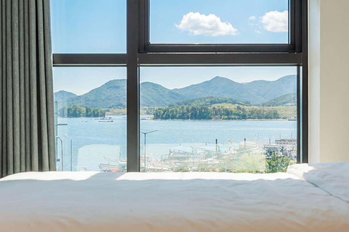 Cama com vista para um lago e montanhas através de uma janela.