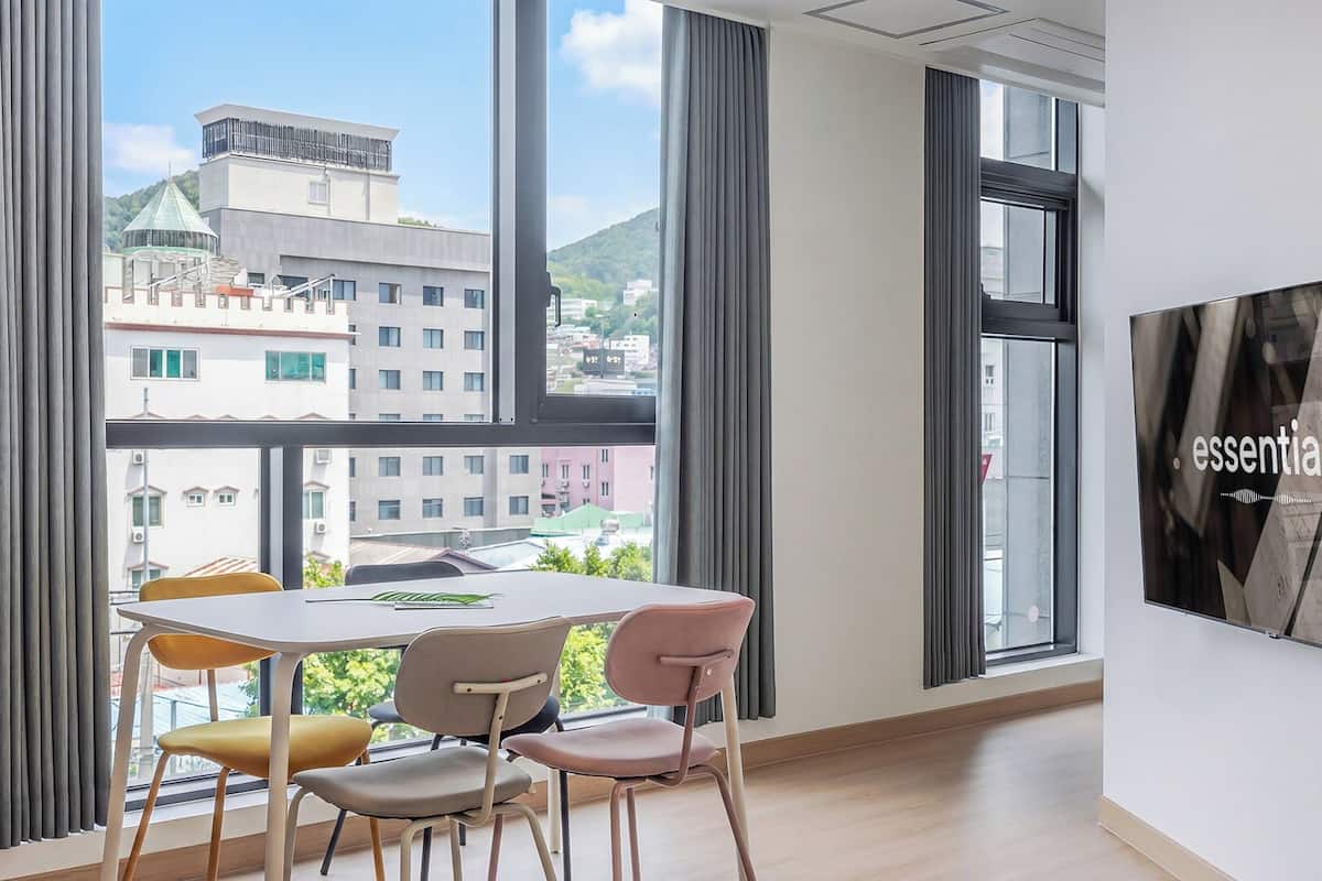 Quarto moderno com uma janela grande, mesa de jantar com cadeiras e TV na parede.