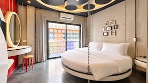 Quarto moderno com cama redonda, penteadeira com espelho e vista para área externa colorida.