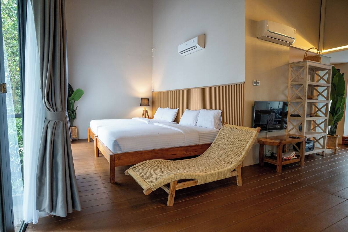 Quarto com cama, poltrona, televisão e ar condicionado.