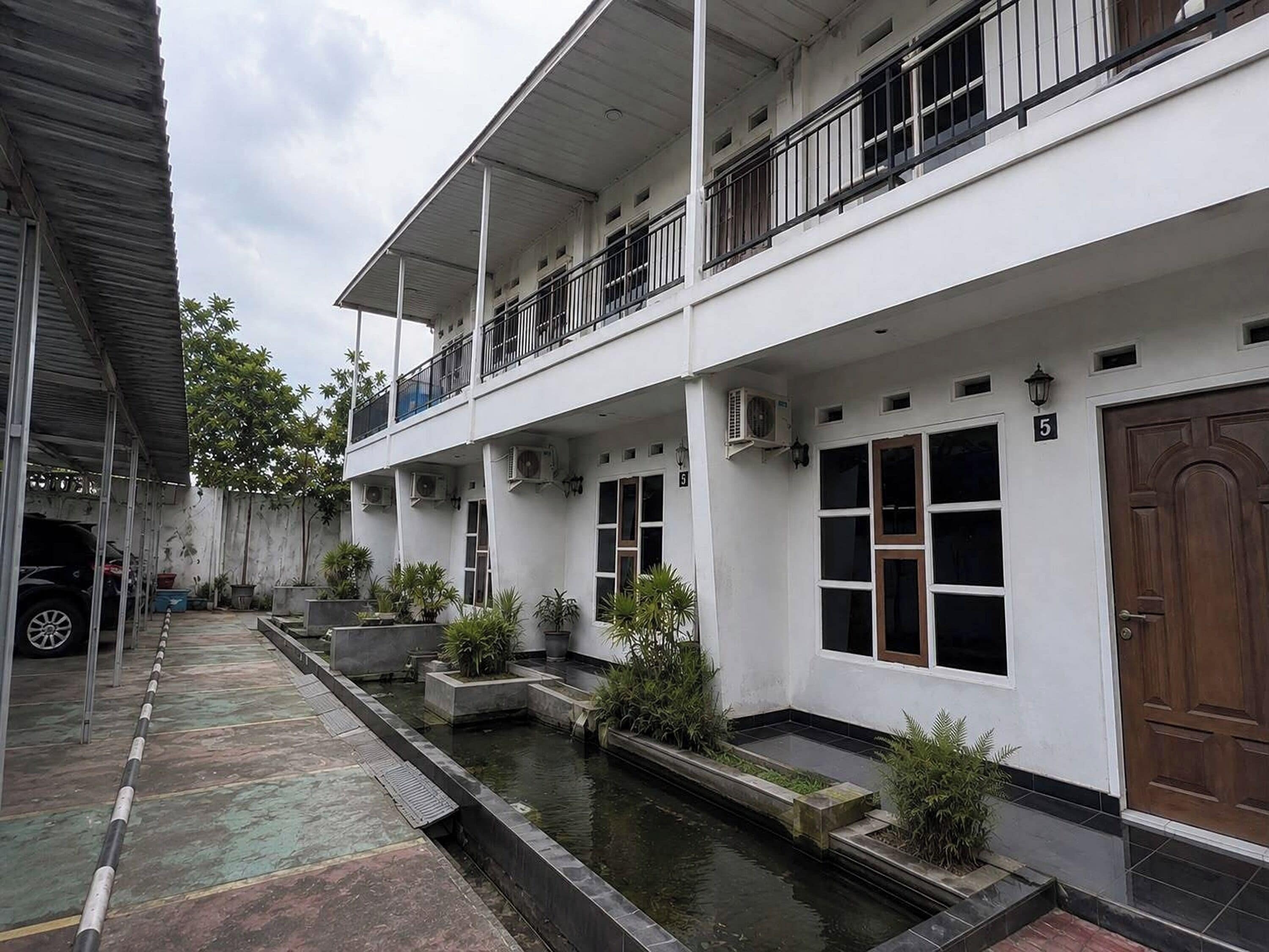 Um edifício de dois andares com galeria coberta, um pequeno espelho d'água e uma placa com o número 5.