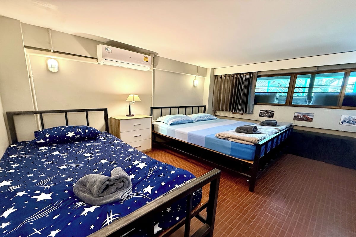 Quarto com cama, mesa de cabeceira, abajur, aparelho de ar condicionado e janela com cortinas.