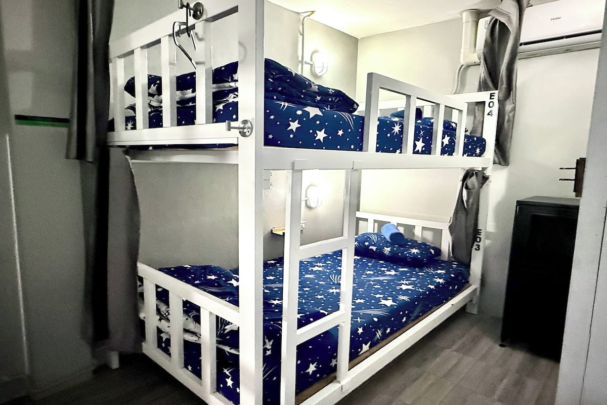 Quarto com beliche, uma pequena escrivaninha e um refrigerador.