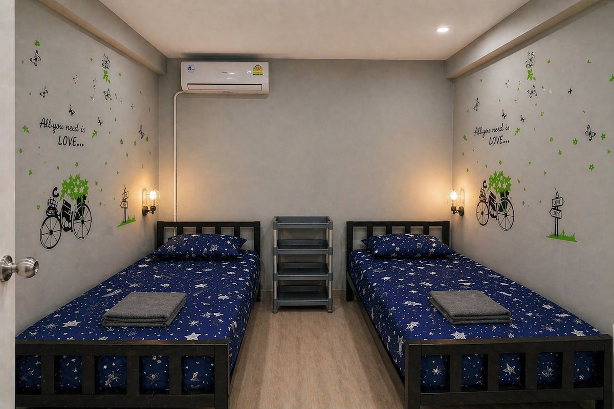 Quarto duplo com duas camas, ar condicionado fixado na parede e adesivos decorativos.
