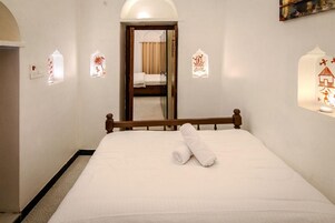 Cama bem arrumada com toalha enrolada, cabeceira de madeira e arandelas decorativas.