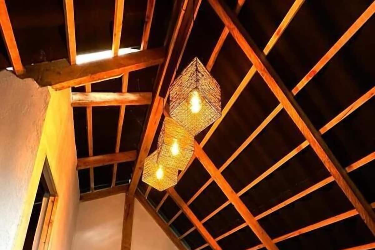 Um quarto com teto inclinado, uma cama com almofadas, uma mesinha de cabeceira e um lustre.