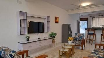 Uma sala de estar com televisão, sofá, cadeiras e um tapete estampado.