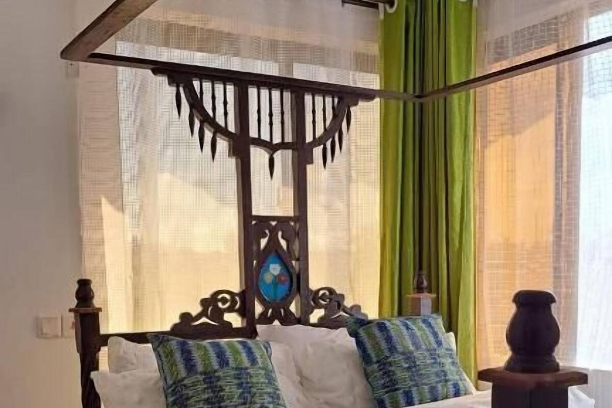 Quarto com cama de dossel, cabeceira de madeira, mesa de cabeceira e criado-mudo.