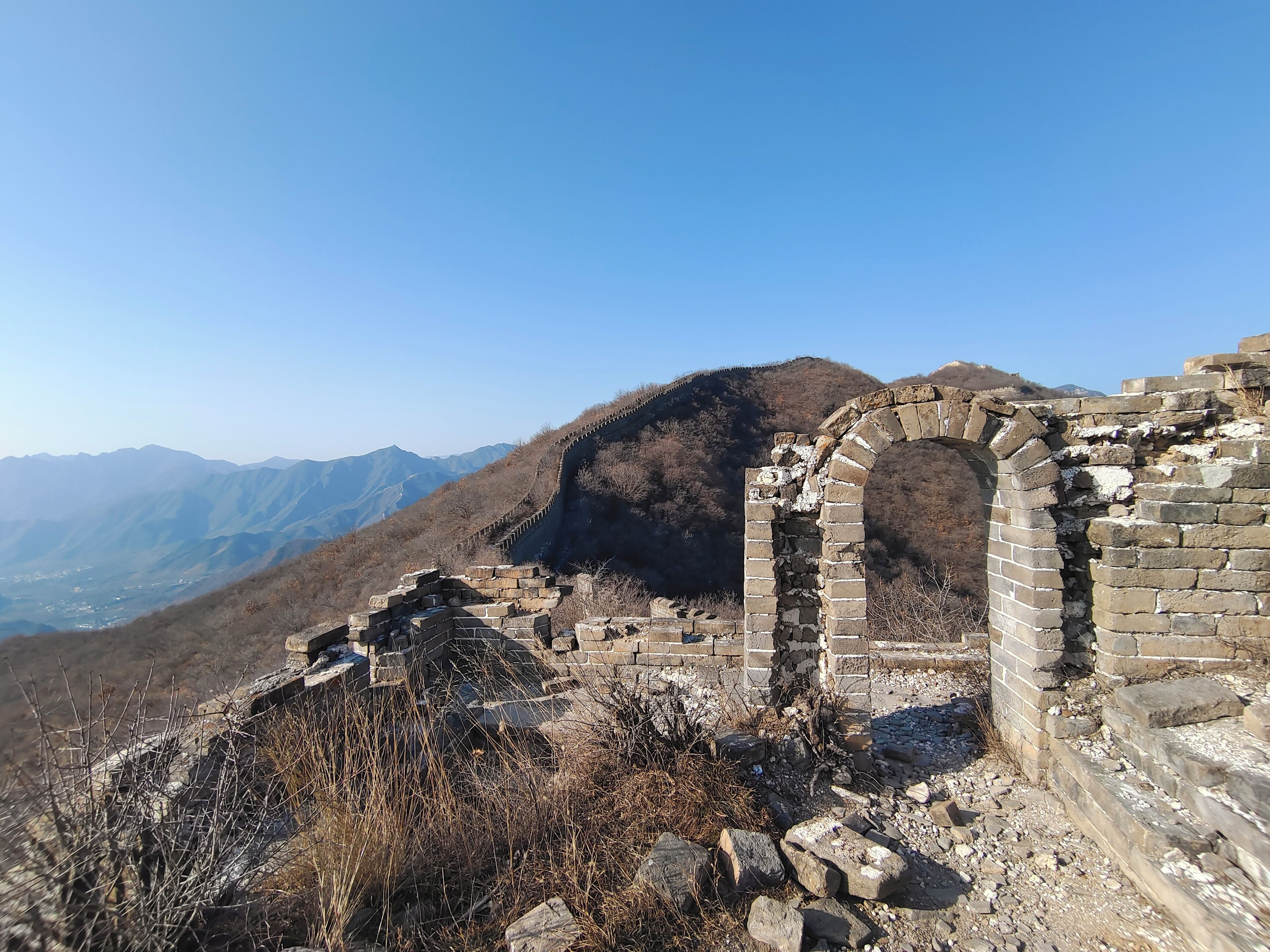 Trecho da Grande Muralha da China com ruínas de pedra e montanhas ao fundo.