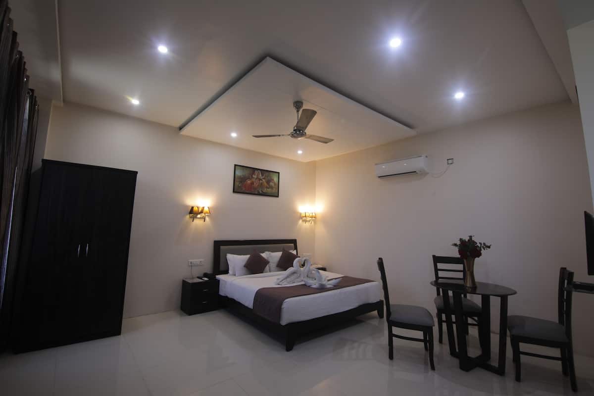 Quarto de hotel com cama, luminárias de cabeceira, ventoinha no teto, uma pequena mesa com cadeiras e aparelho de ar condicionado.