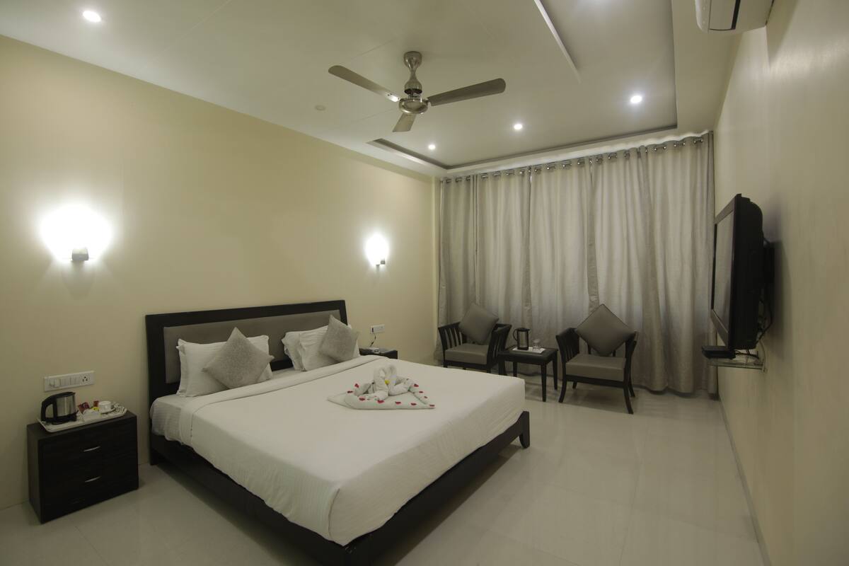 Quarto de hotel com cama, ventoinha no teto, televisão, escrivaninha e cadeira.