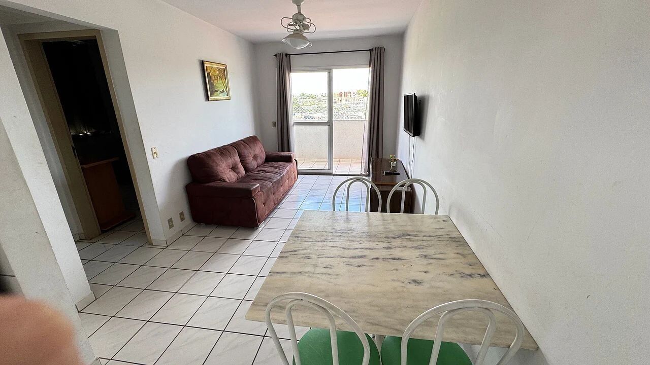 Quarto com sofá, mesa de jantar com cadeiras, televisão e porta de vidro deslizante para área externa.