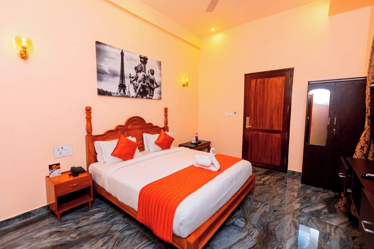 Quarto de hotel com cama, mesa de cabeceira, porta de madeira e um quadro na parede.