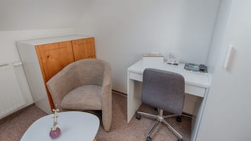 Quarto com escrivaninha branca, duas cadeiras, uma mesinha com um vaso e um radiador.