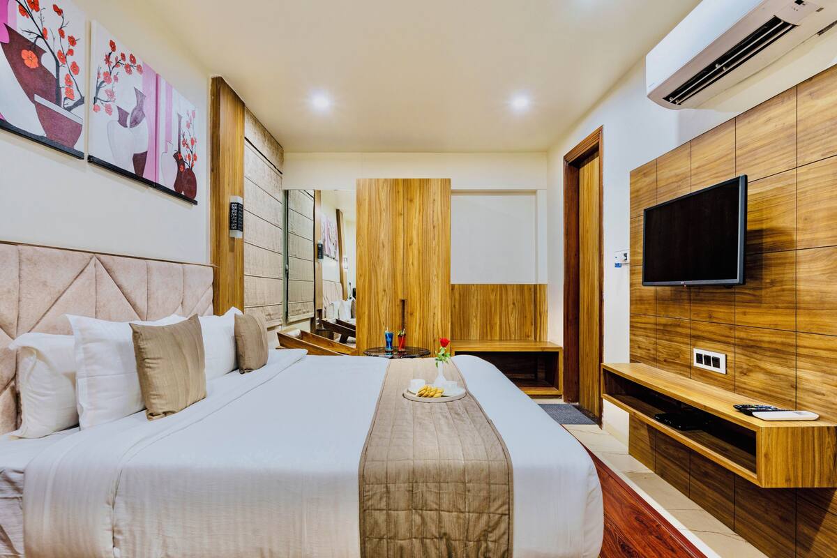 Quarto de hotel com cama, televisão, parede de painéis de madeira e um quadro.