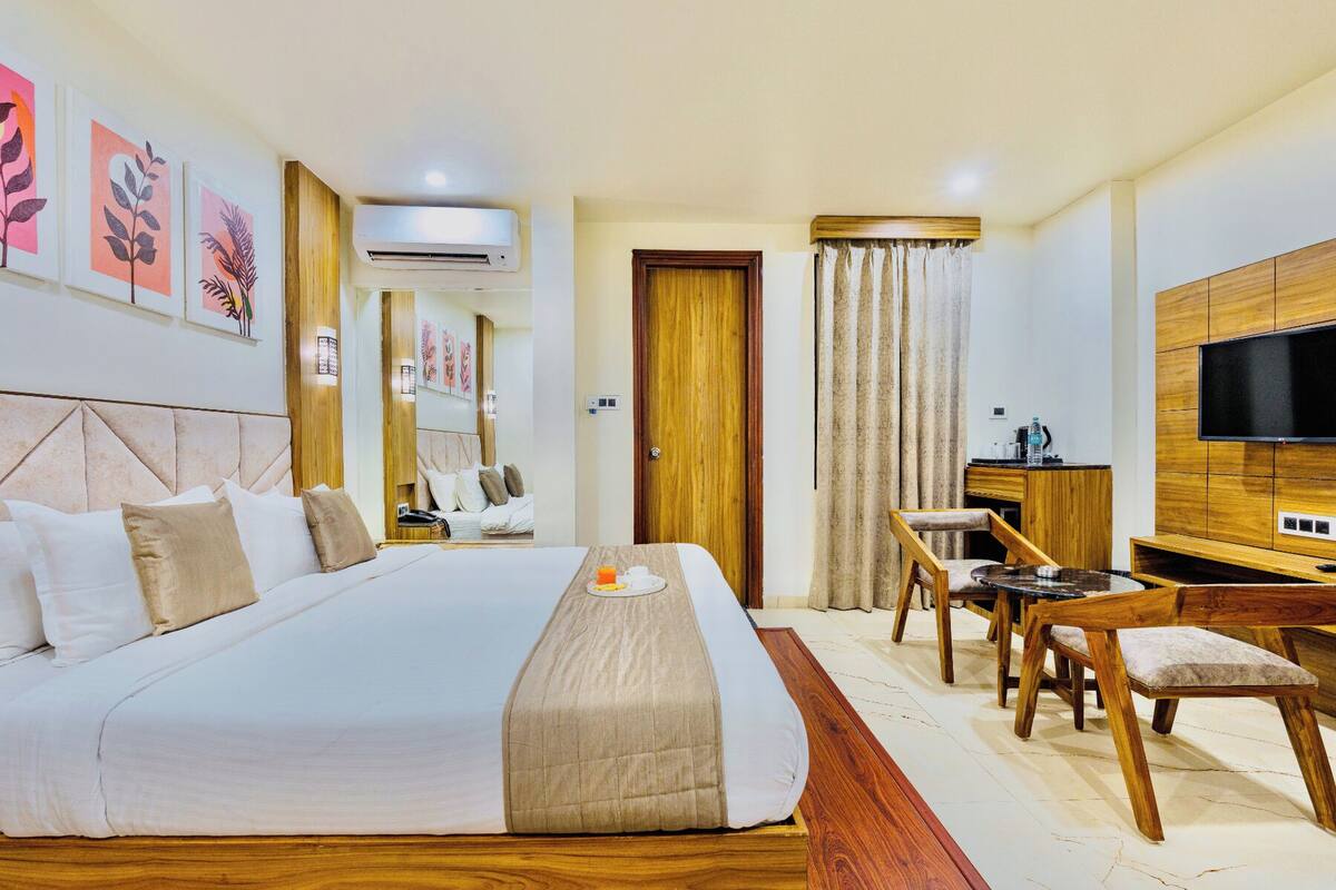 Quarto de hotel com uma cama grande, uma escrivaninha com cadeira, televisão e obras de arte nas paredes.