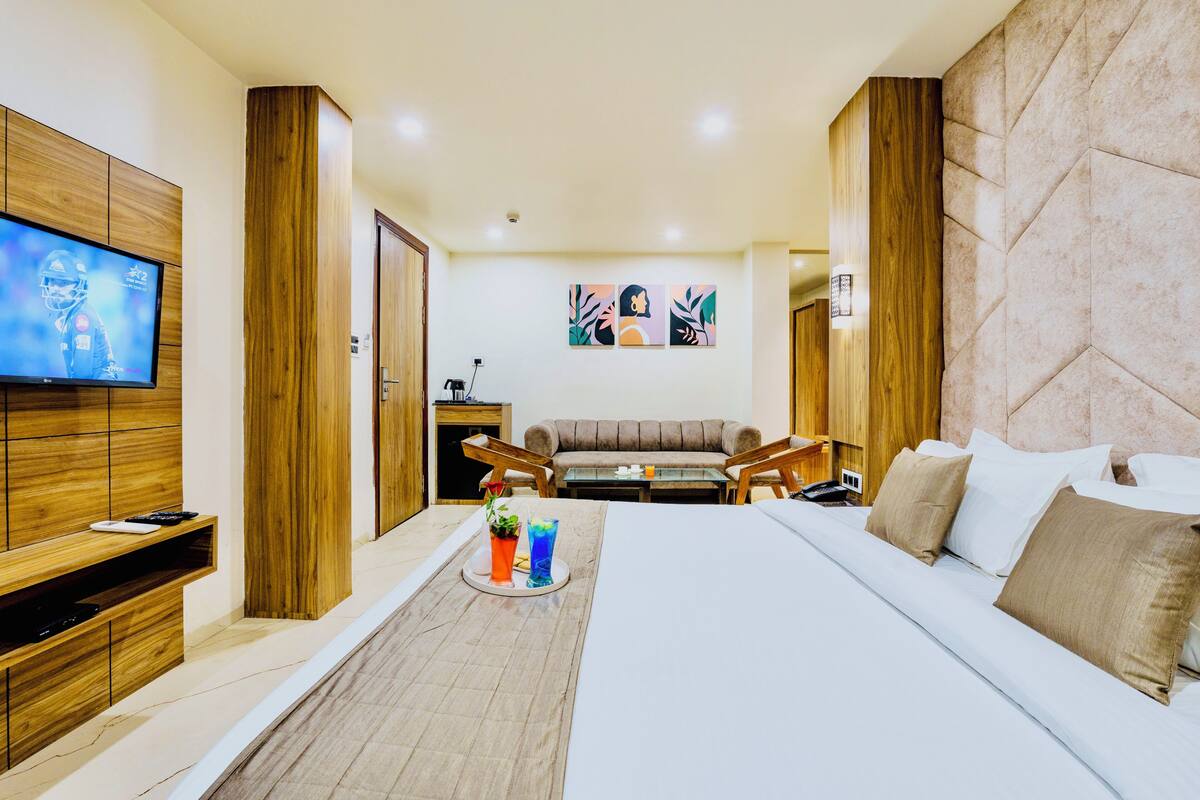 Quarto de hotel com cama, televisão, sofá, mesa de centro e obras de arte na parede.