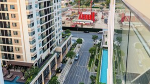 Um edifício alto com piscina no terraço, área ajardinada bem cuidada e rua movimentada abaixo.