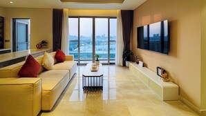 Uma sala de estar moderna com sofá, mesa de centro, TV e vista para a cidade através de janelas amplas.