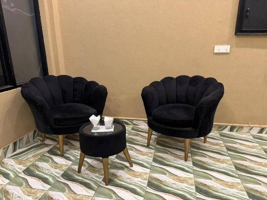 Duas poltronas pretas com pés de madeira, uma mesinha redonda com um porta-lenços, e um piso estampado.