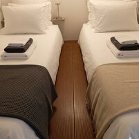 Quarto de hotel com duas camas, cada uma com lençóis brancos e toalha dobrada.