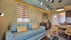 Sala de estar com sofá, mesinha de centro, área de refeições com cadeiras, uma bicicleta e cozinha ao fundo.