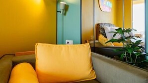 Quarto com sofá, luminária na parede e reflexo de uma cama com almofadas.