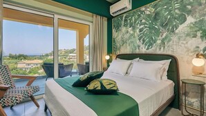 Quarto de hotel com uma cama grande, vista para o mar, varanda com uma cadeira e pintura de parede com tema tropical.