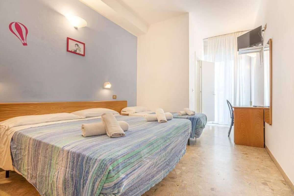 Quarto de hotel com duas camas, uma escrivaninha, uma cadeira, uma televisão e uma janela com cortinas.