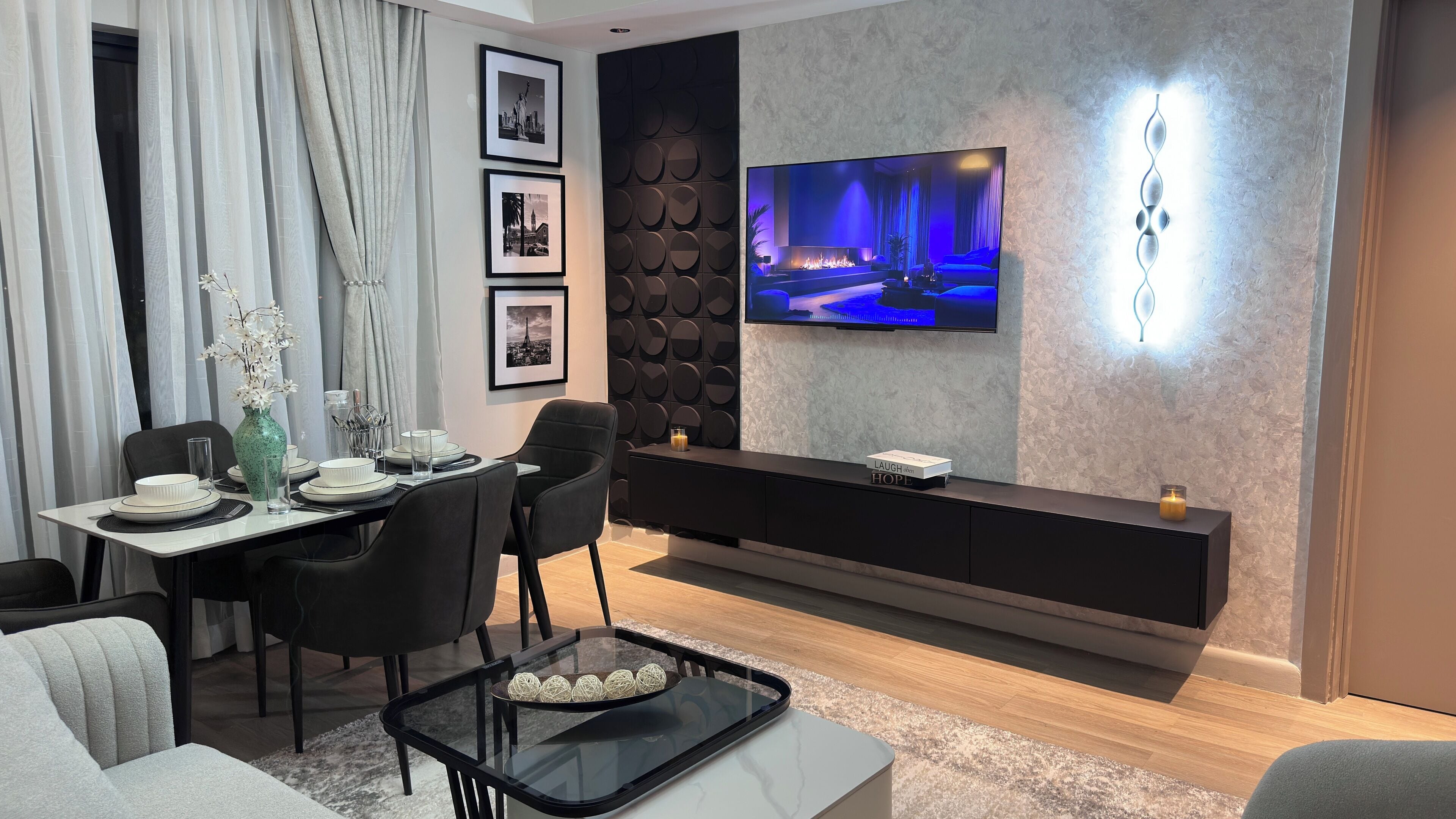 Uma sala de estar moderna com área de jantar, televisão de tela plana e painel decorativo na parede.
