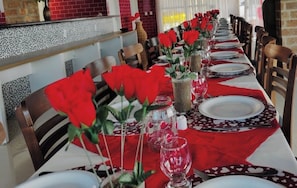 Uma mesa de jantar comprida posta com rosas vermelhas, pratos brancos e copos de vidro transparente.