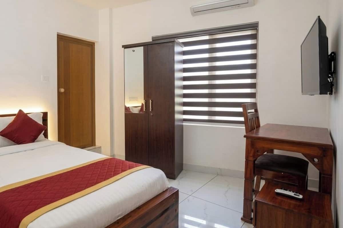 Quarto de hotel com cama, escrivaninha, guarda-roupa e janela com persianas.