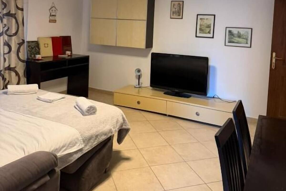 Quarto com cama, televisão, escrivaninha e guarda-roupa.