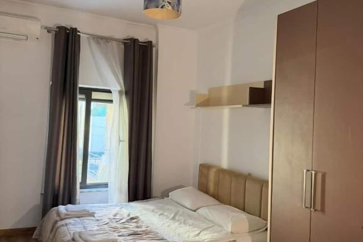 Quarto com cama, guarda-roupa, luminária no teto e janela com cortinas.