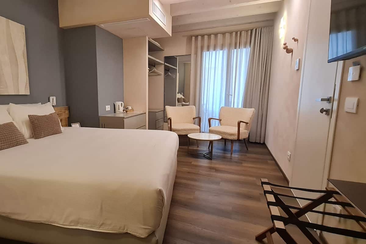 Quarto de hotel com uma cama grande, uma mesinha, duas cadeiras, um espelho e uma televisão.