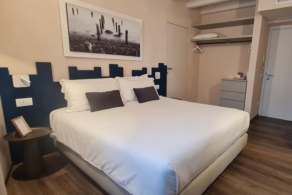 Quarto com cama, mesa de cabeceira, luminária na parede e porta para um armário.