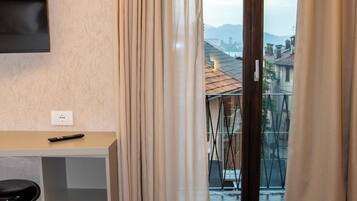 Quarto de hotel com cama, escrivaninha, televisão e varanda com cortinas.