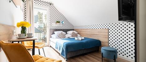 Um quarto com cama, escrivaninha, cadeira, uma pequena mesa com flores e uma planta em vaso.